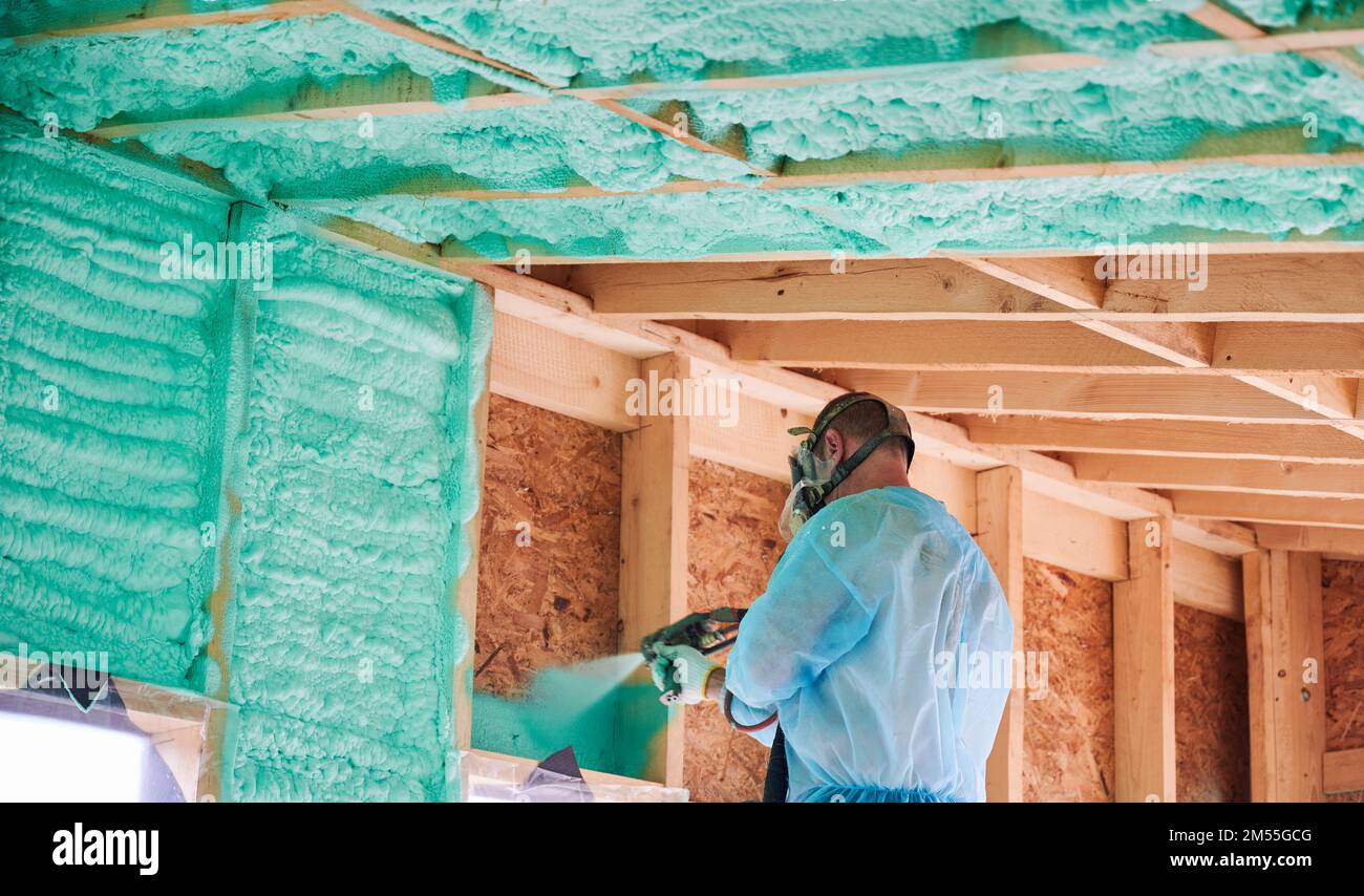 Male builder insulating wooden frame house. Man worker spraying ...