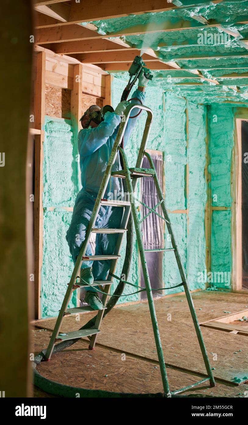 Male builder insulating wooden frame house. Man worker spraying ...