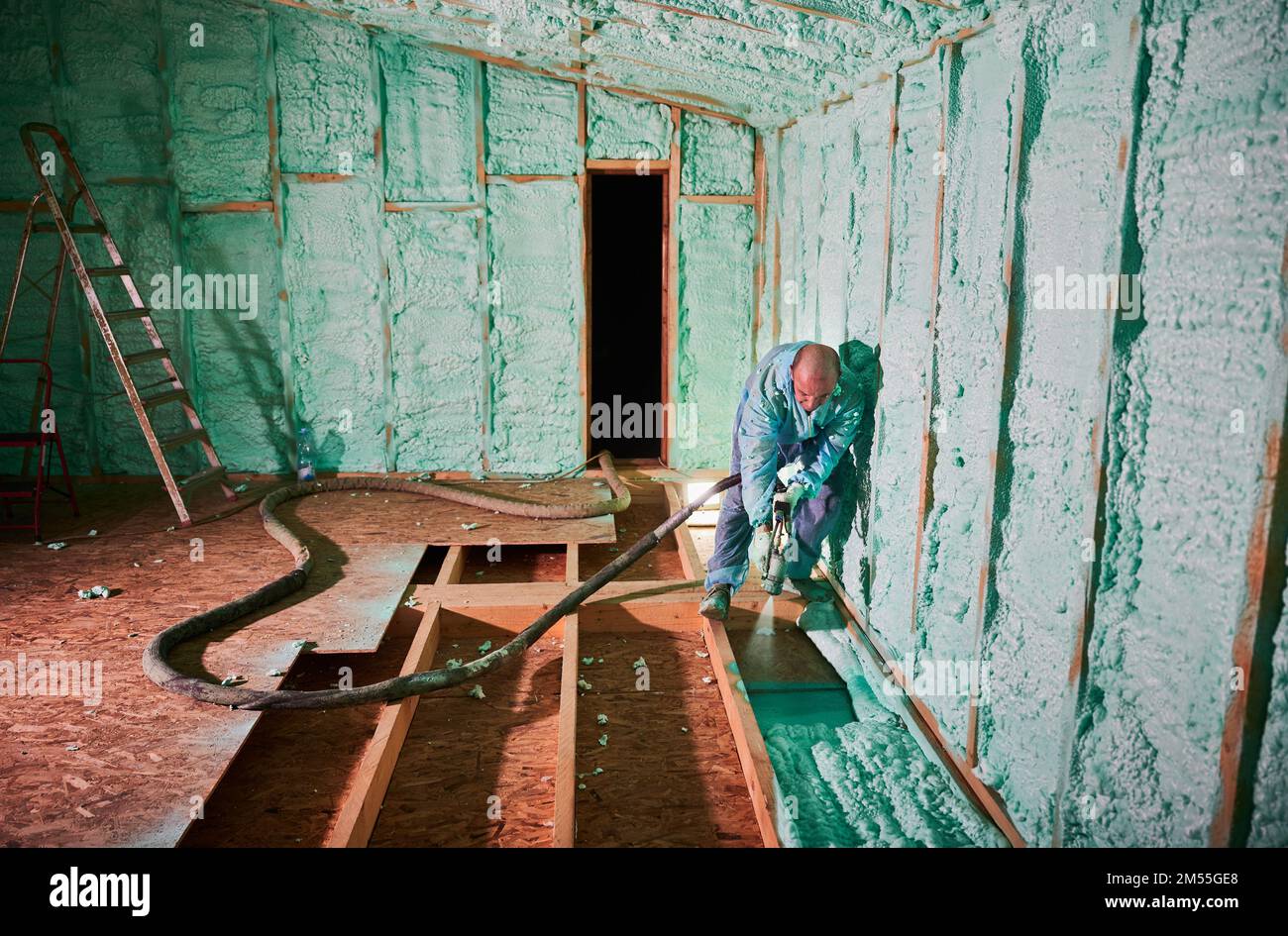 Male builder insulating wooden frame house. Man worker spraying ...