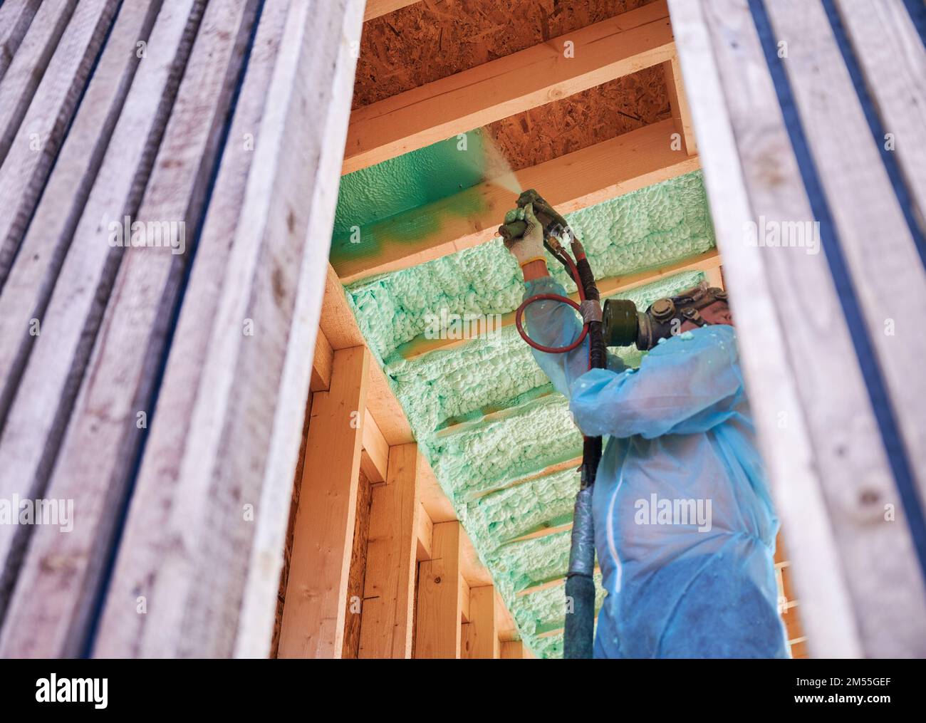 Male builder insulating wooden frame house. Man worker spraying ...