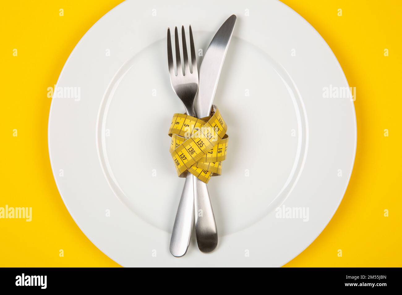 fork and knife tied with tape measure on white plate. flat lay diet ...
