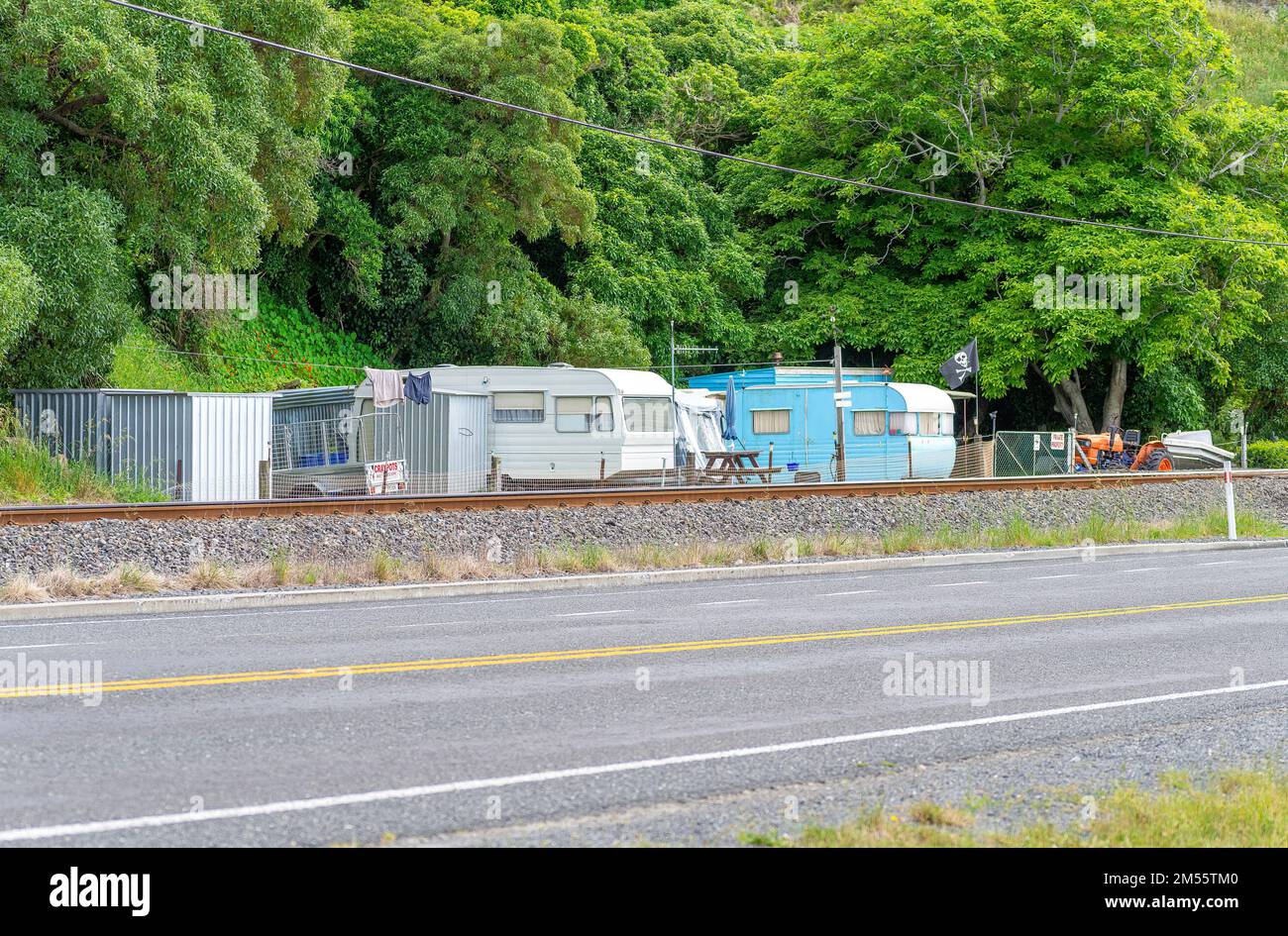 A row of camper vans parked at a campsite by the road and railway in ...