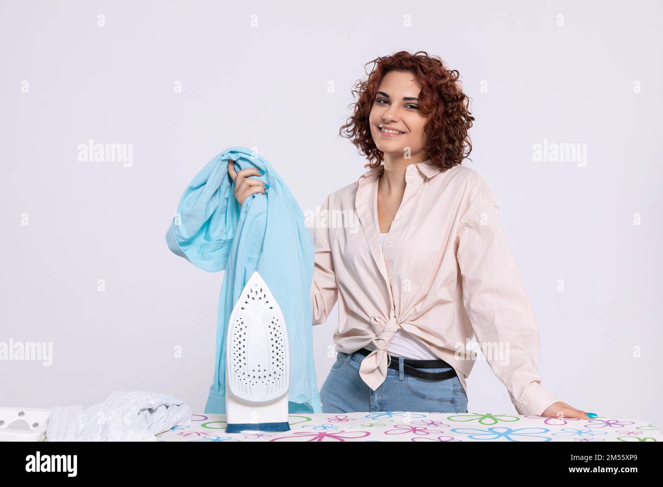 The girl smiles gratefully while standing by the ironing board and iron ...