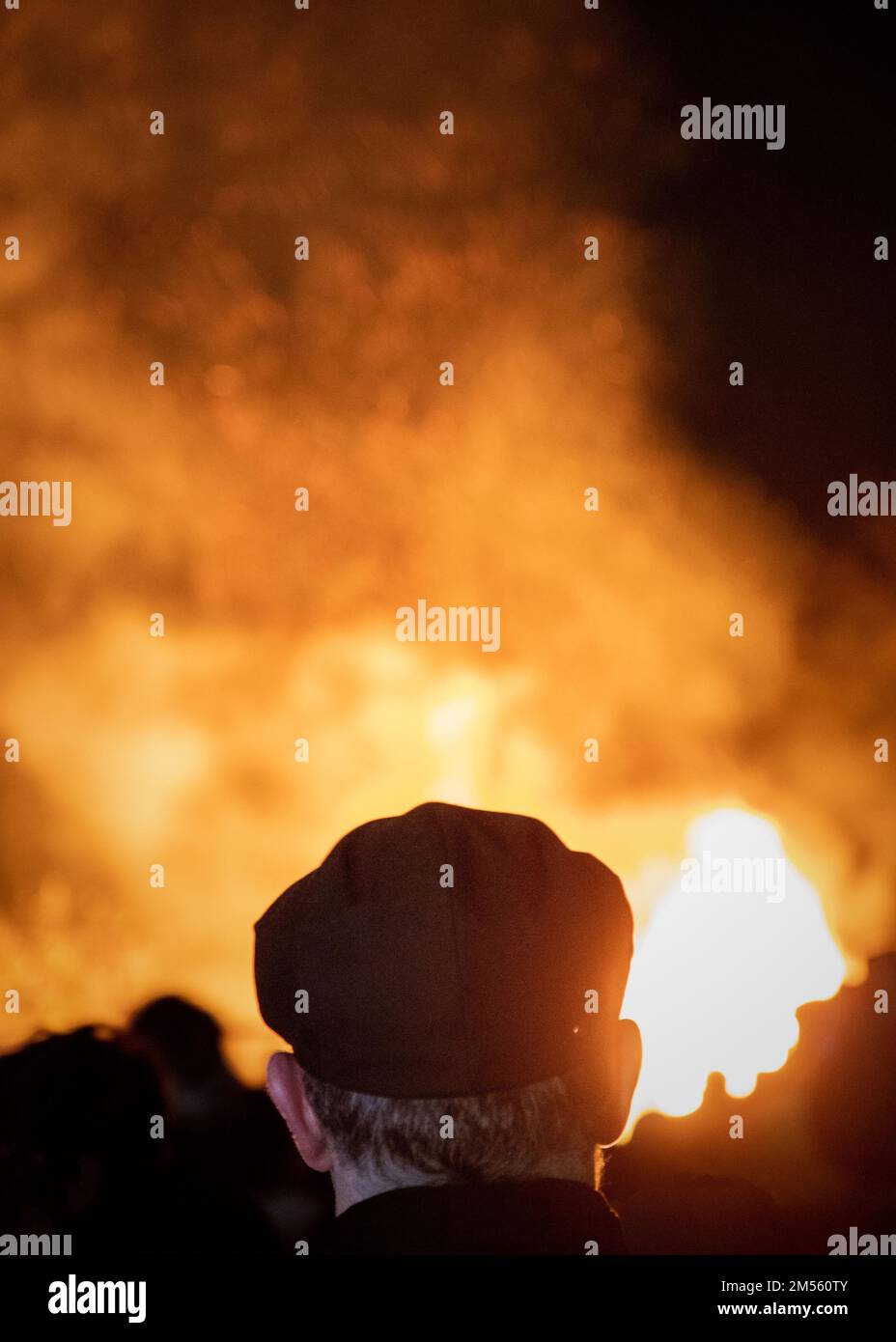 A vertical view of the crowd standing before the roaring bonfire flames ...