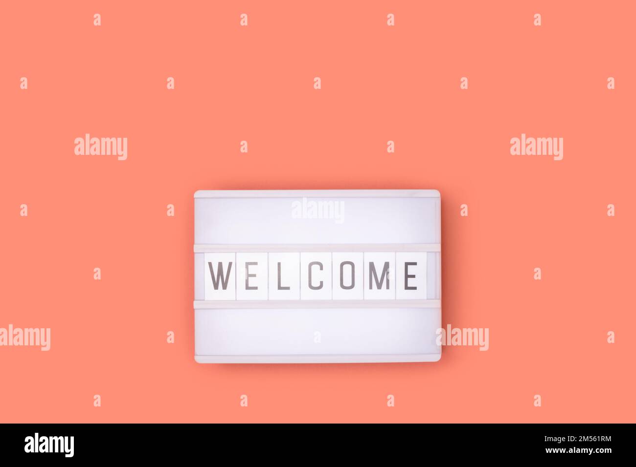 Word Welcome. White lightbox with letters on a coral colored background ...