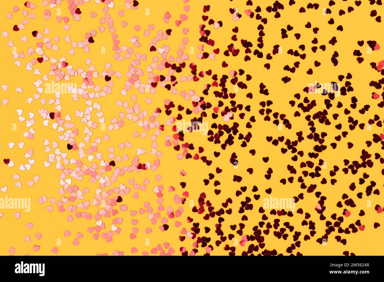 Metallic red confetti in a heart shaped scattered on a yellow ...
