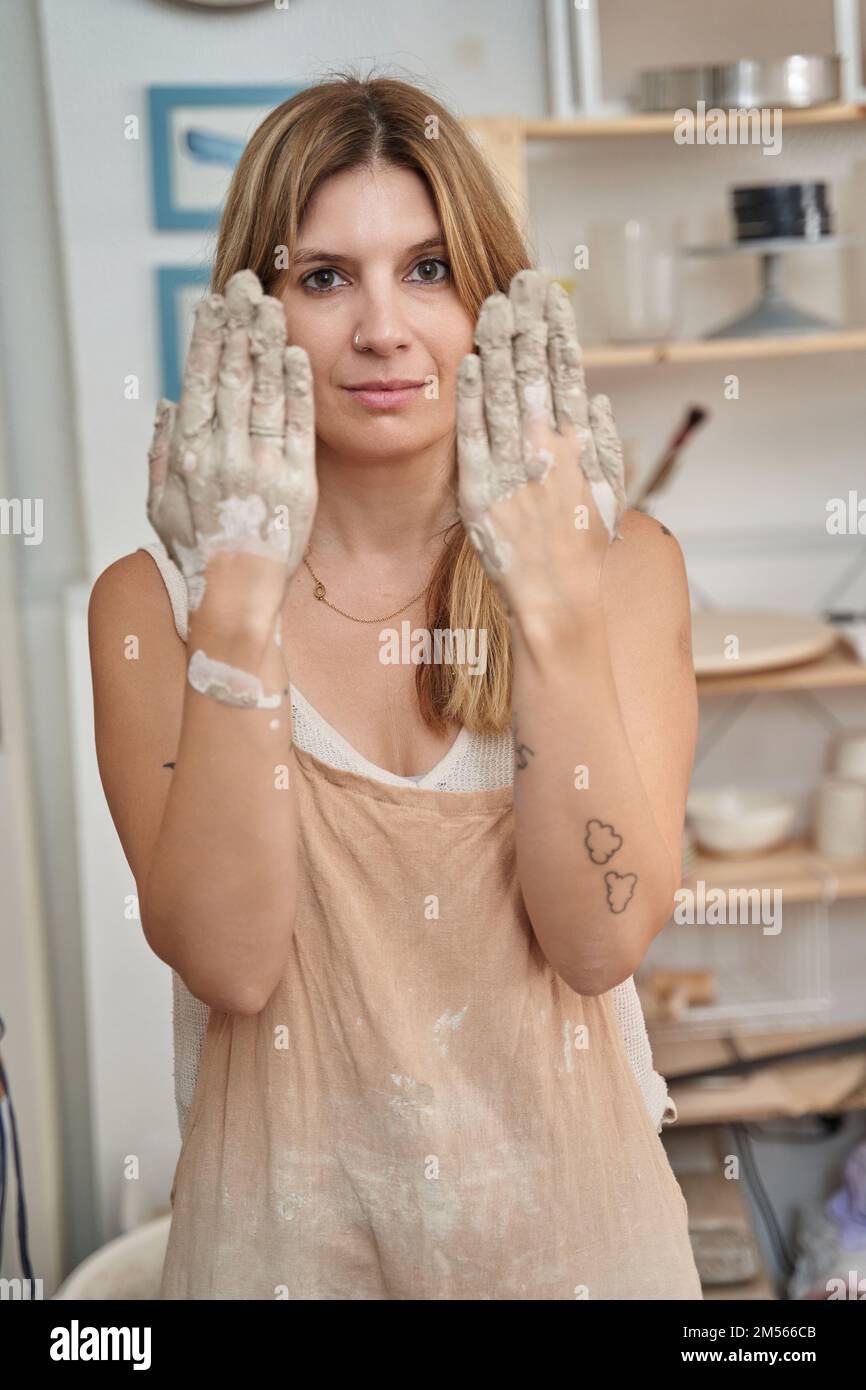 Woman looking at camera and showing hands with clay after working in ...