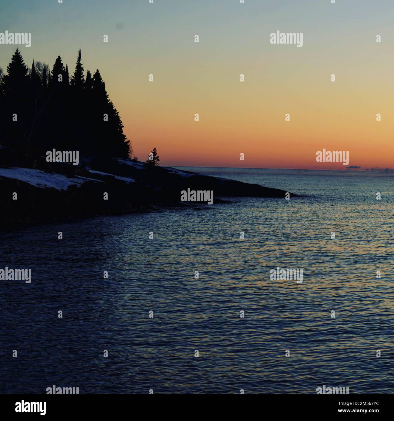 A scenic view of a shoreline with trees and a beautiful sunset in the ...