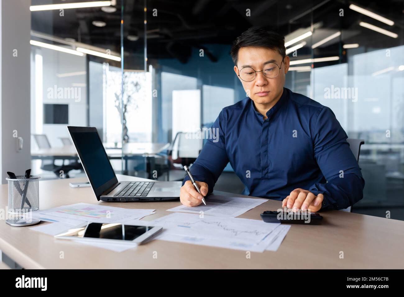 Portrait of a serious young Asian accountant, banker. Sits working in ...