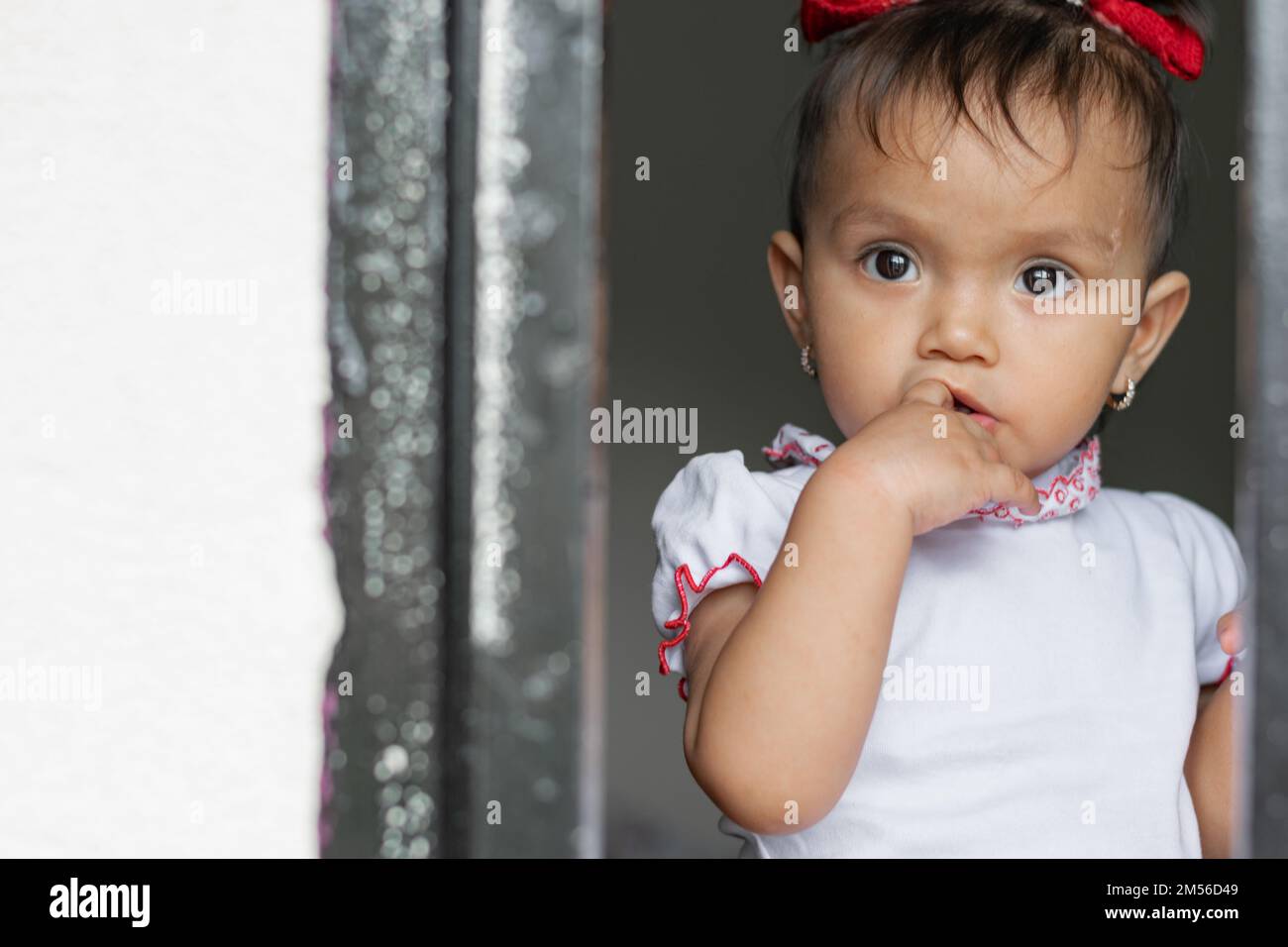 dark-haired baby, looking out the window curiously, one finger stuck in ...