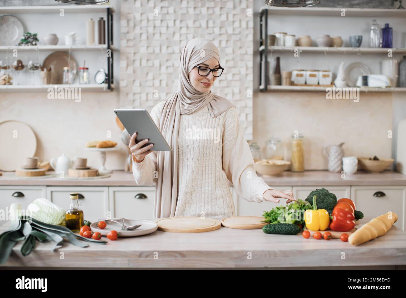 Happy muslim woman in hijab cooking healthy food pointing on vegetables ...