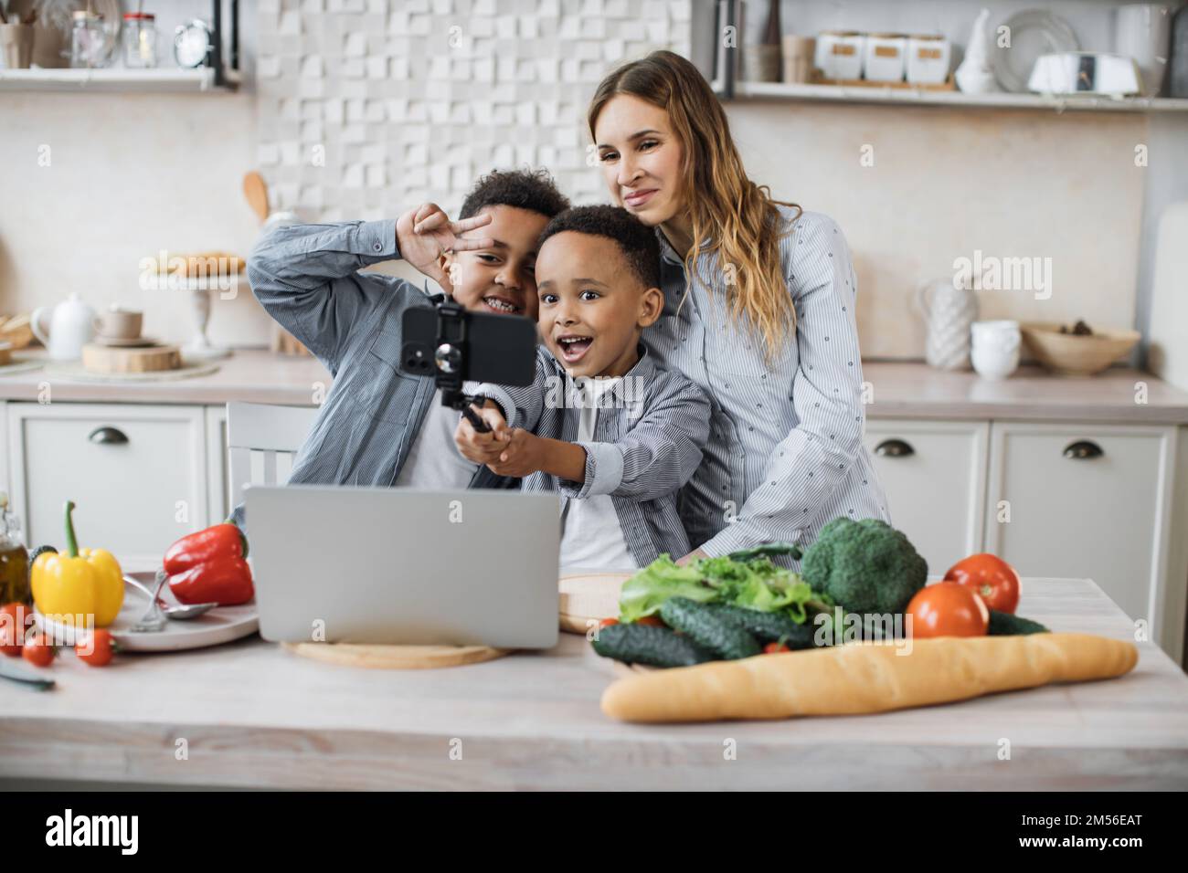 Pretty young mother and two children sons preparing salad with fresh ...