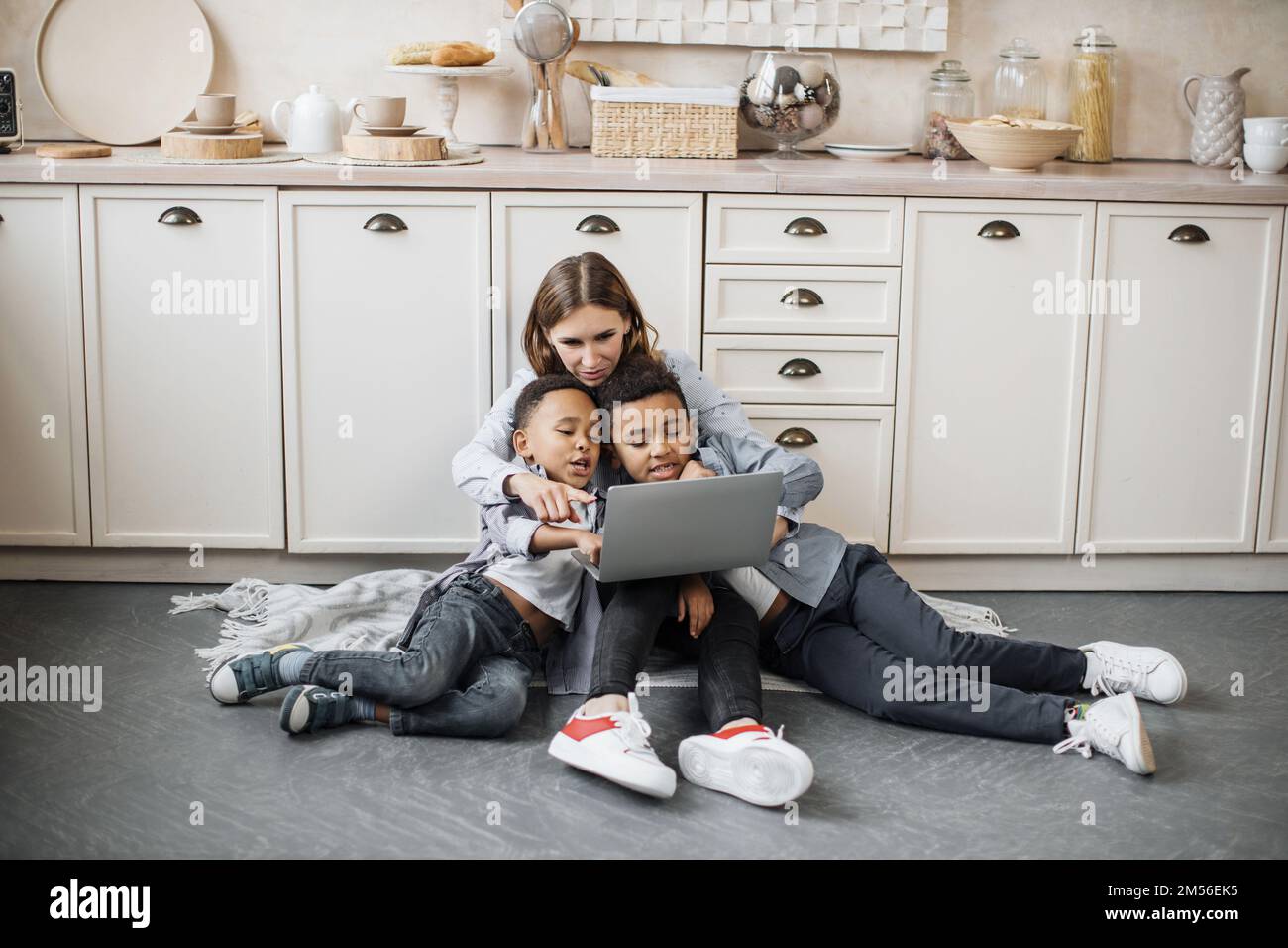 Smiling caucasian mother and two african children sons sitting on warm ...