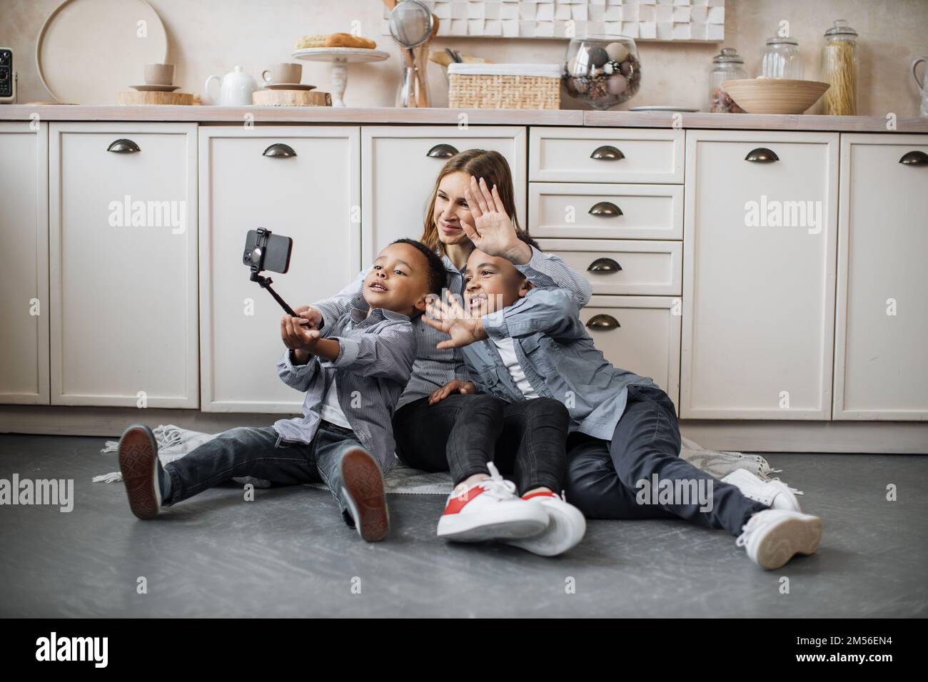 Happy multinational family of mother and two sons sitting on warm floor ...