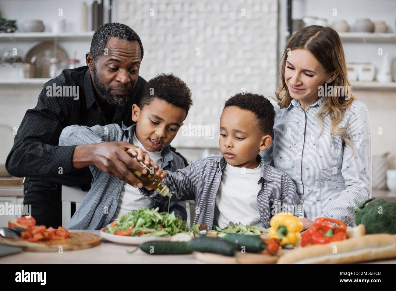 Portrait of smiling mom, dad and little sons adding olive oil to the ...