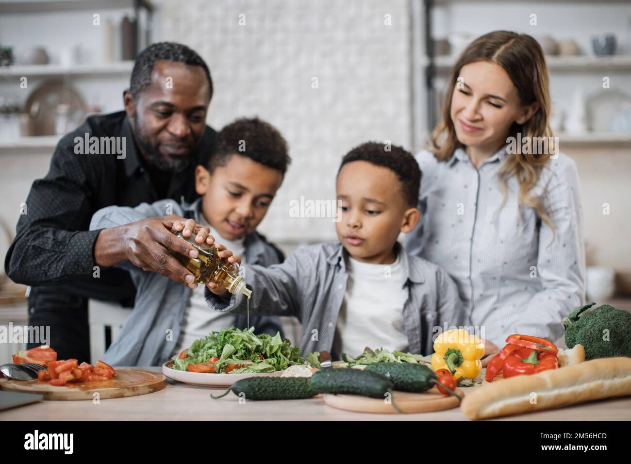Portrait of smiling mom, dad and little sons adding olive oil to the ...