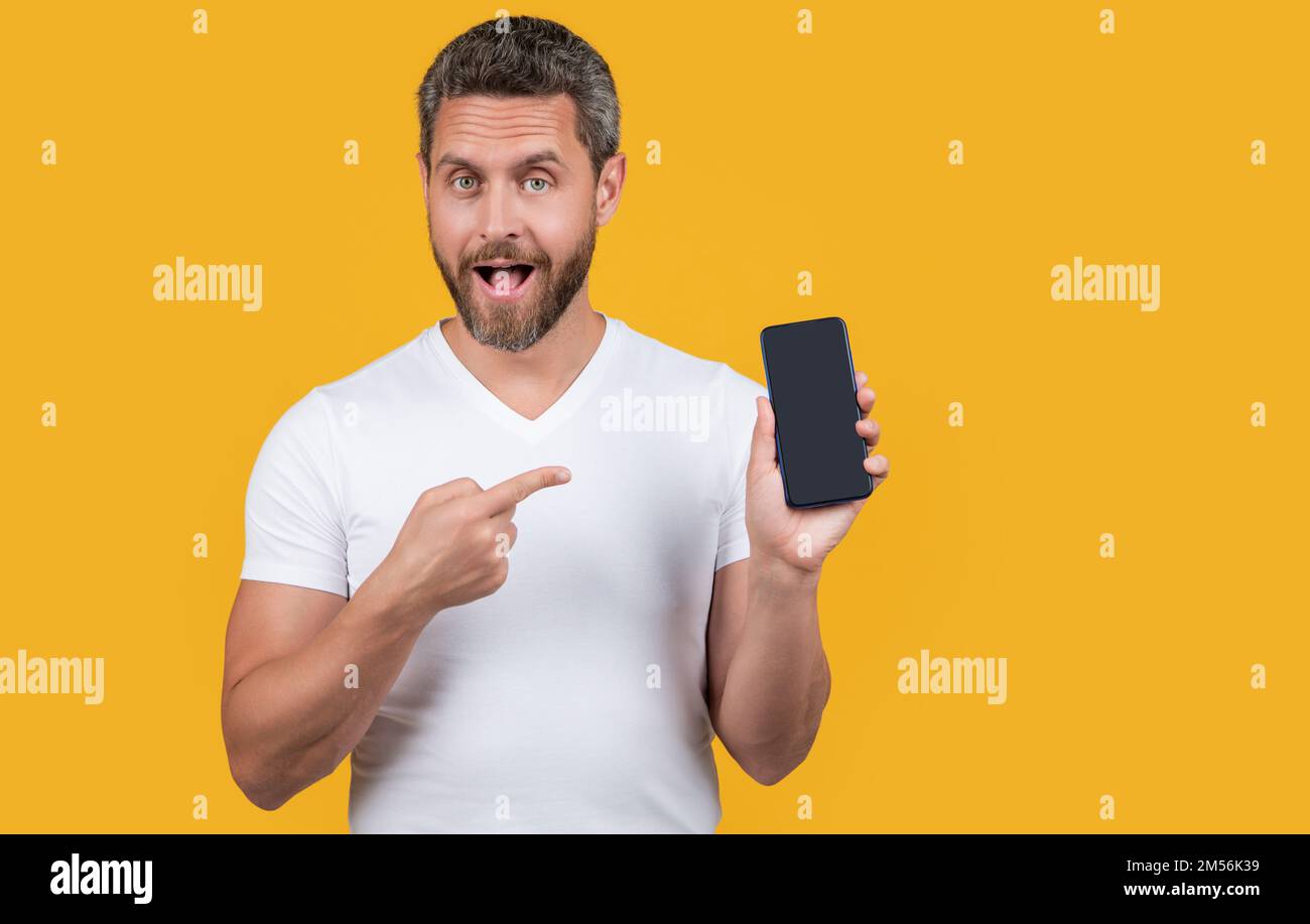 amazed man showing phone screen isolated on yellow background. man ...