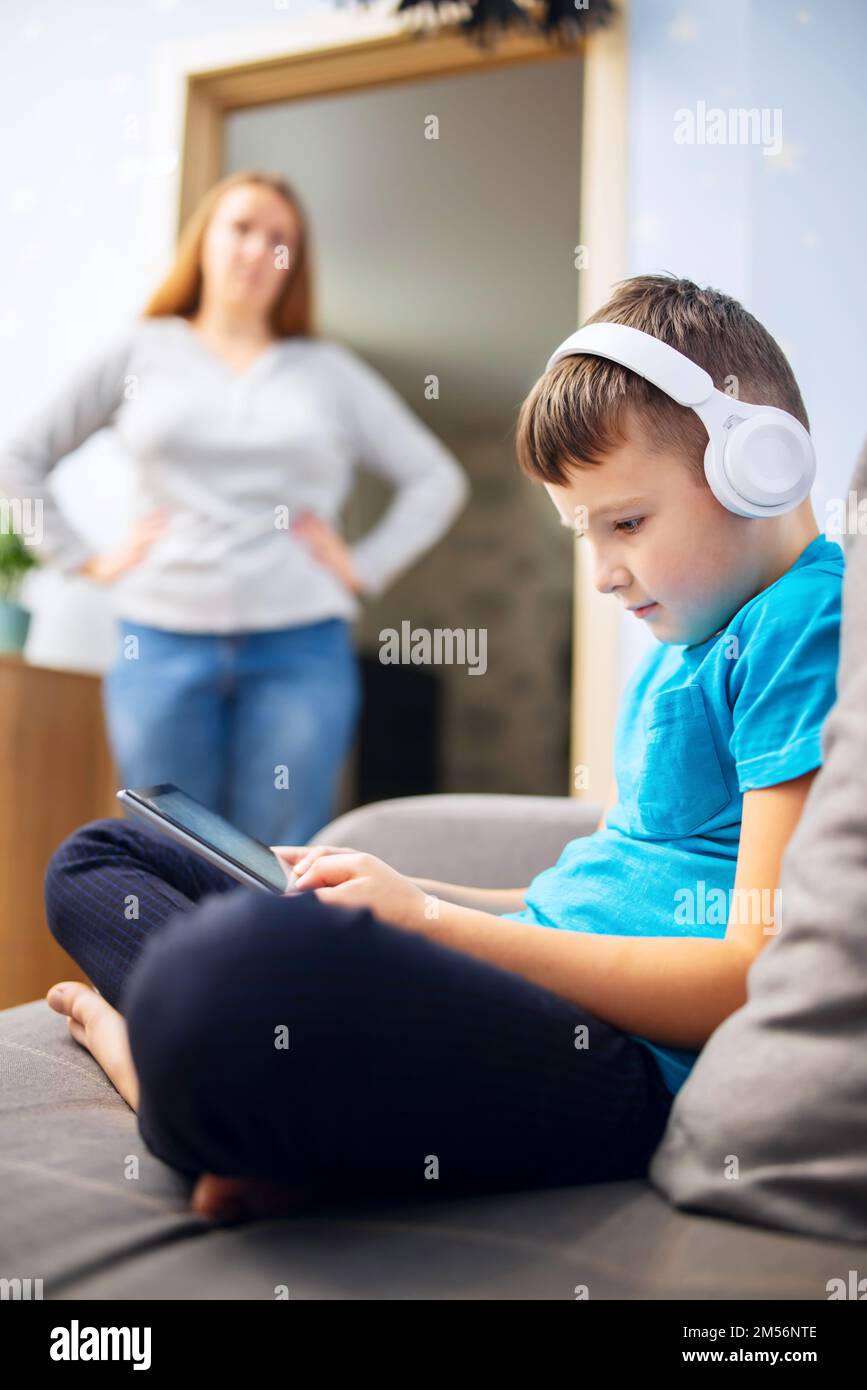 Mother scolds her son. Boy uses tablet with headphones and ignores his ...