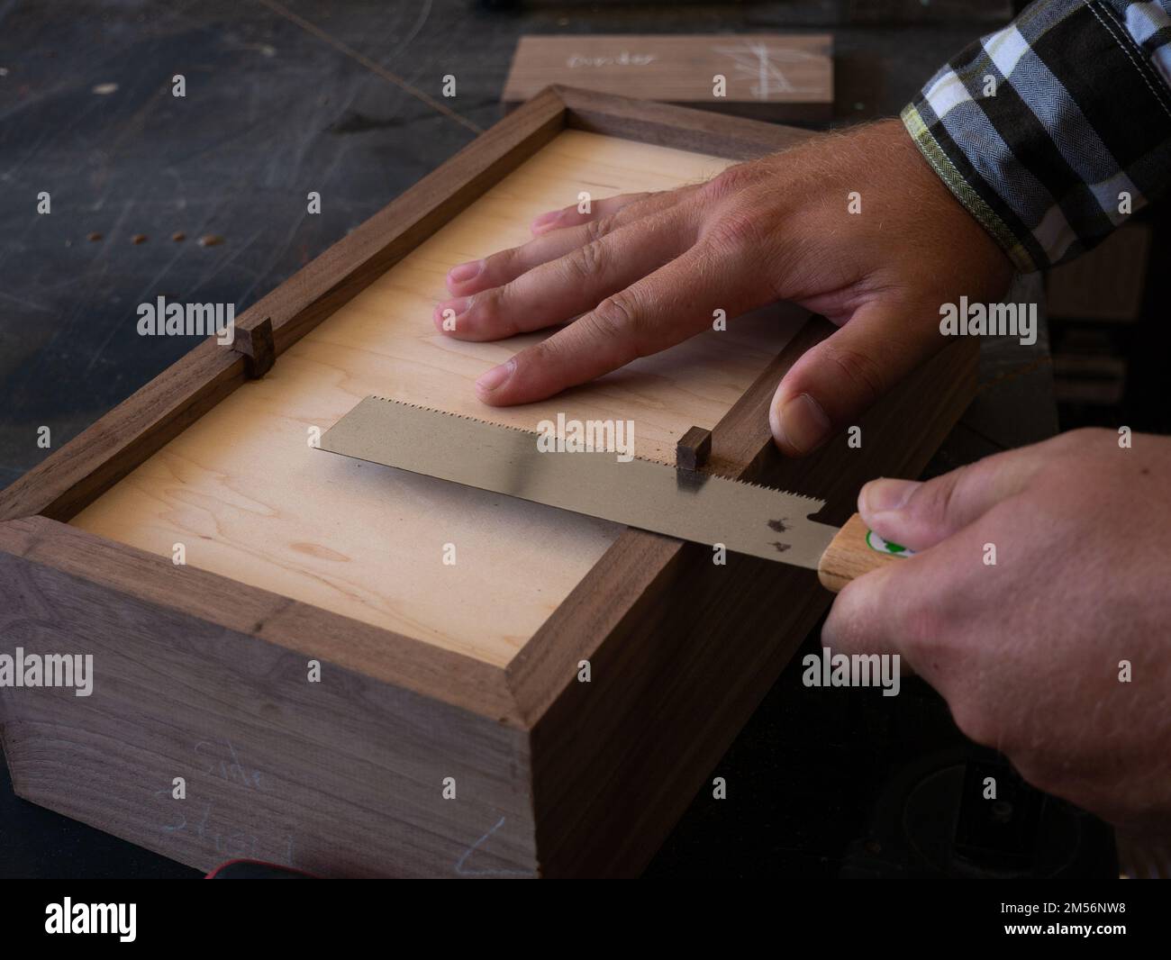 A carpenter sawing off the extra wood off the box he is building in his ...