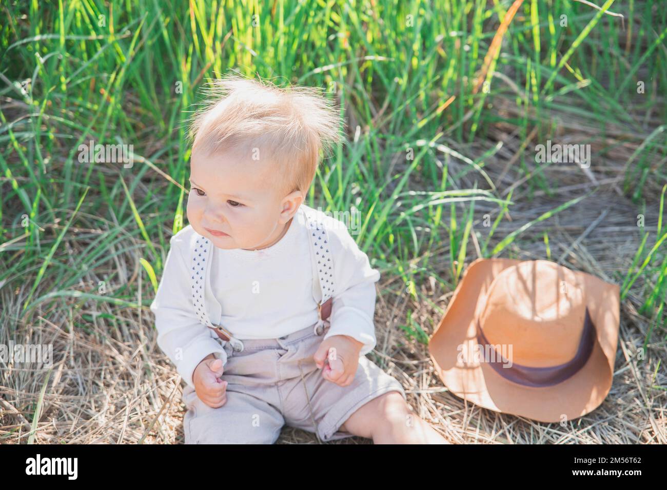 charming baby in a hat and suspenders in the field Stock Photo - Alamy