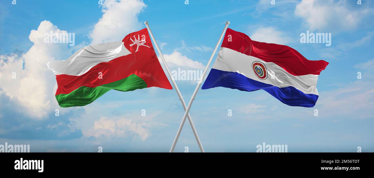 two crossed flags Paraguay and Oman waving in wind at cloudy sky ...