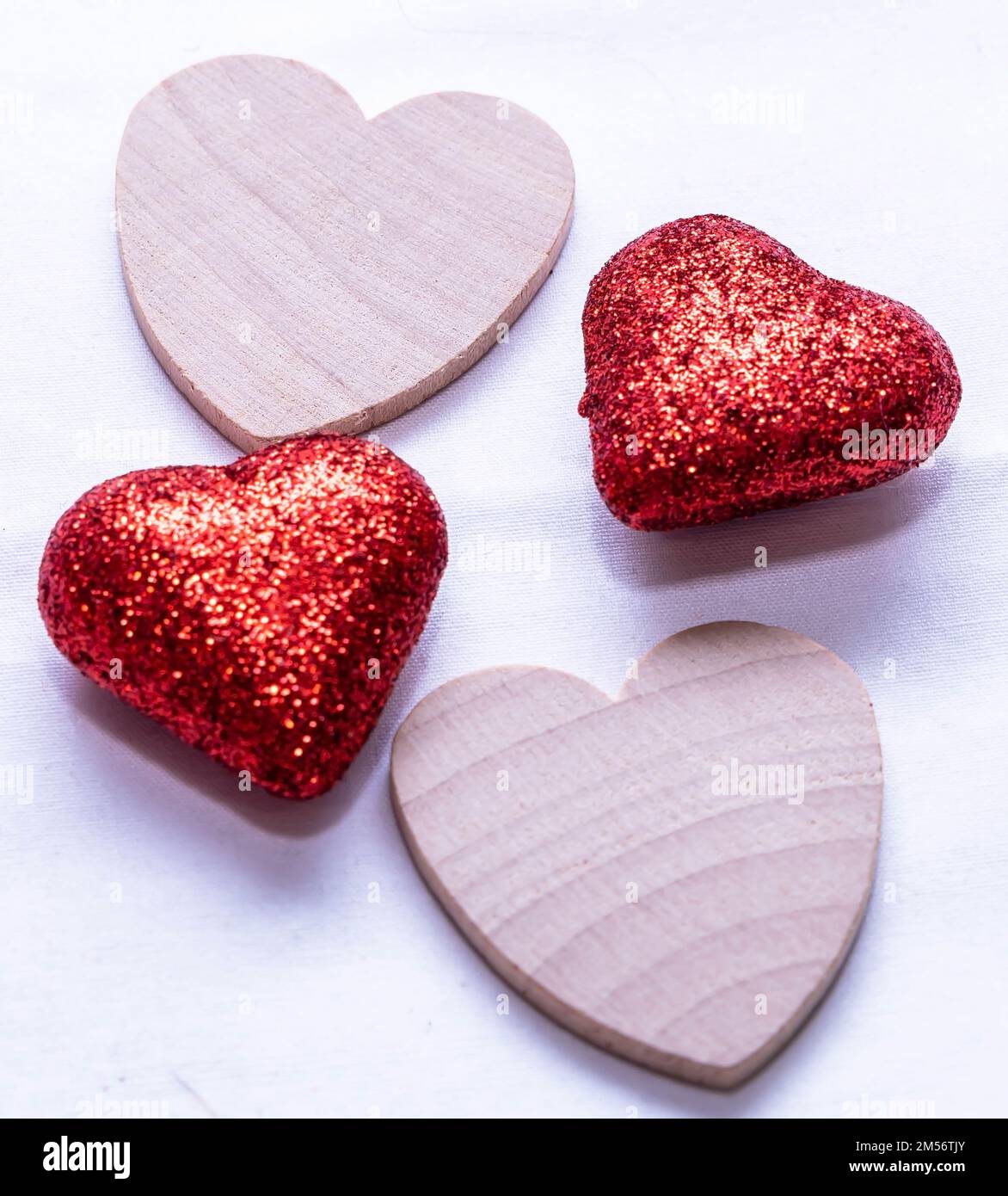 Two red glitter hearts with two plain wooden hearts together on a white ...