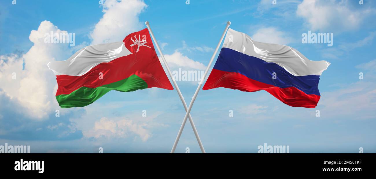 two crossed flags Russia and Oman waving in wind at cloudy sky. Concept ...
