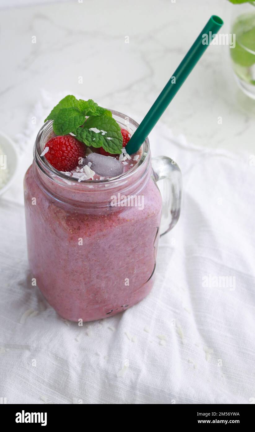 raspberry coconut smoothie with ice in a jar with straw, white ...