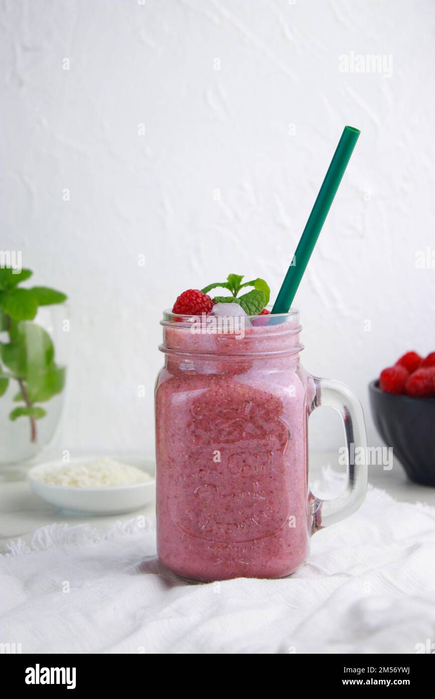 raspberry coconut smoothie with ice in a jar with straw, white ...