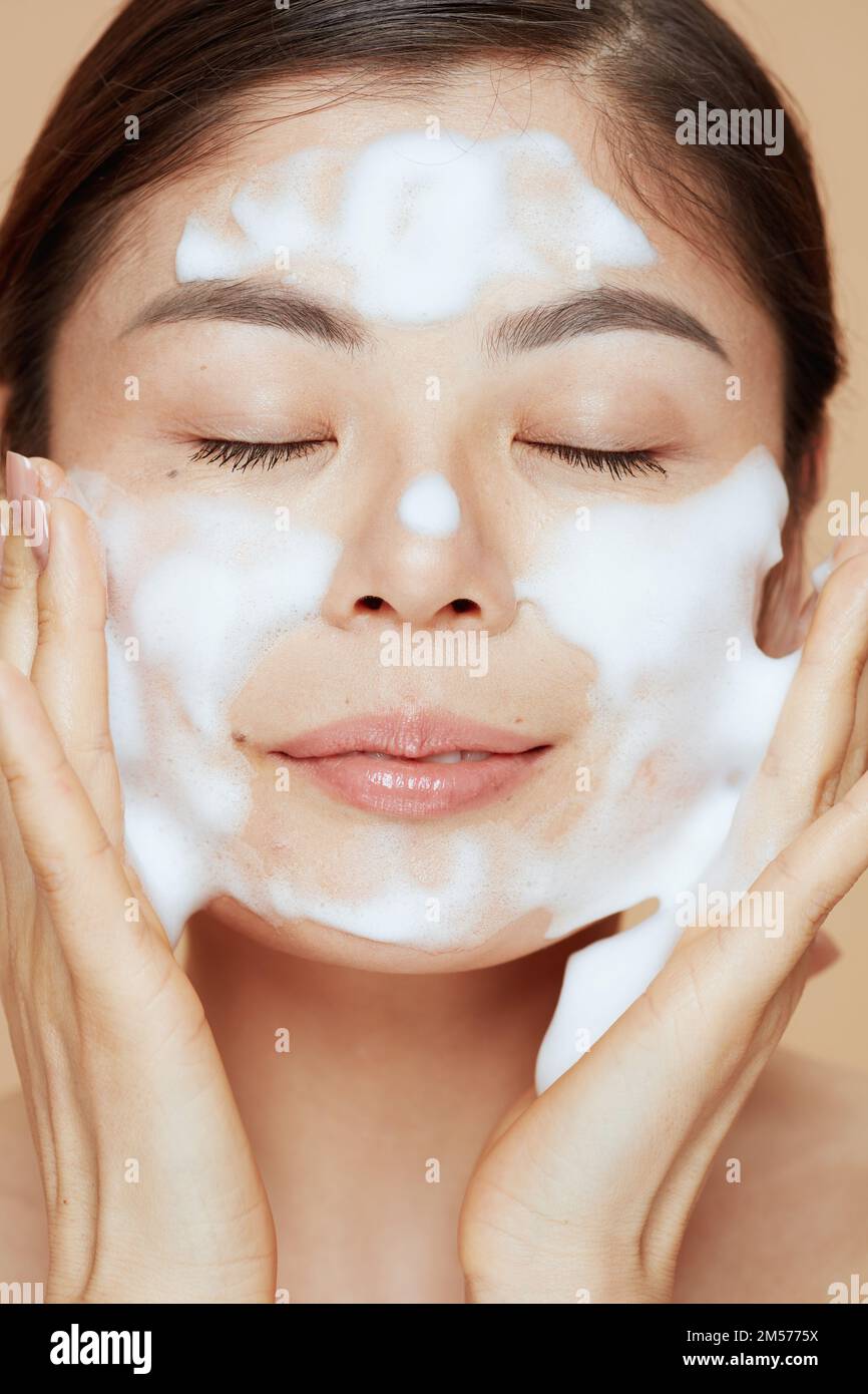 relaxed modern asian female washing face on beige background Stock ...