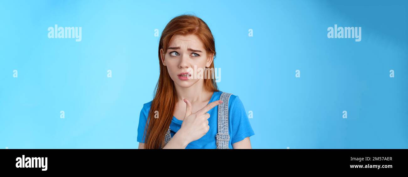 Stupified redhead hesitant girl show aversion, pointing looking left ...