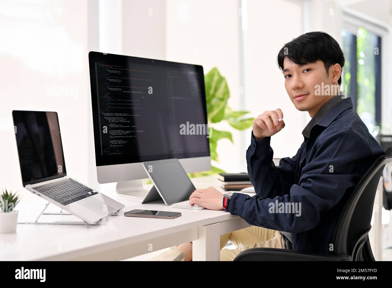 Smart and successful young Asian male web developer sits at his modern ...