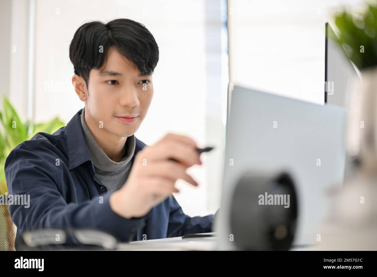Smart and determined young Asian male programmer or web developer working at his office desk ...
