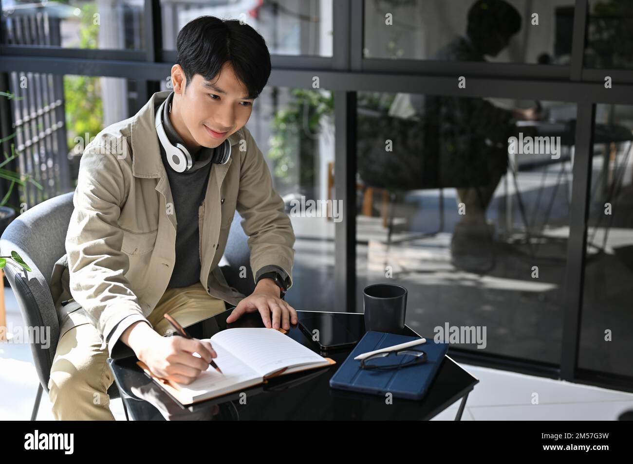 Happy and handsome young Asian man making lists on his personal planner ...