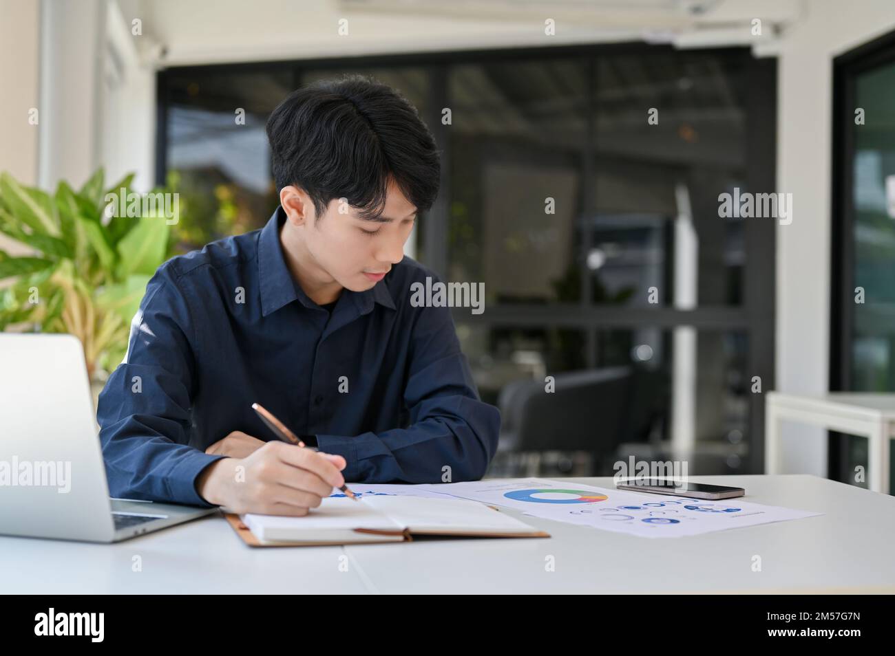 Focused young Asian male financial analyst or accountant working on ...