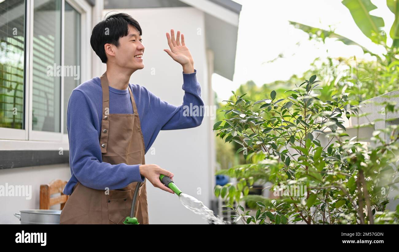 Happy and cheerful young Asian man waving hand, greeting his neighbor ...