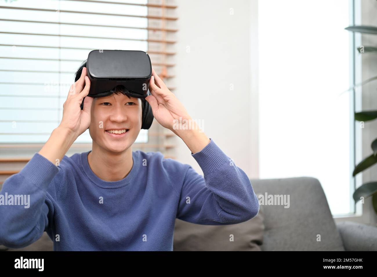 Joyful young Asian man wearing VR glasses, playing VR game in his ...