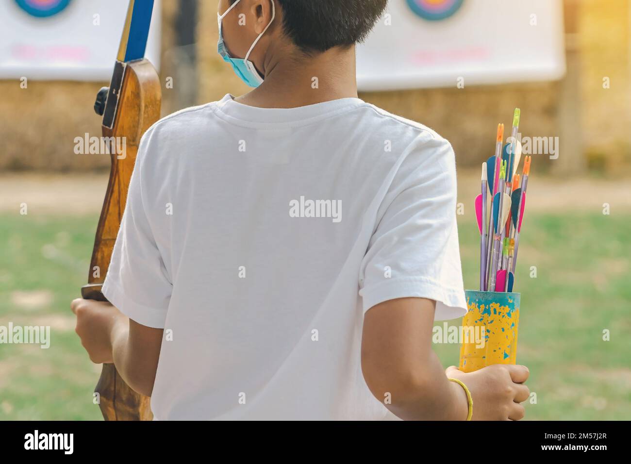 Back view of Asian boy wear face mask aims archery bow and arrow to ...