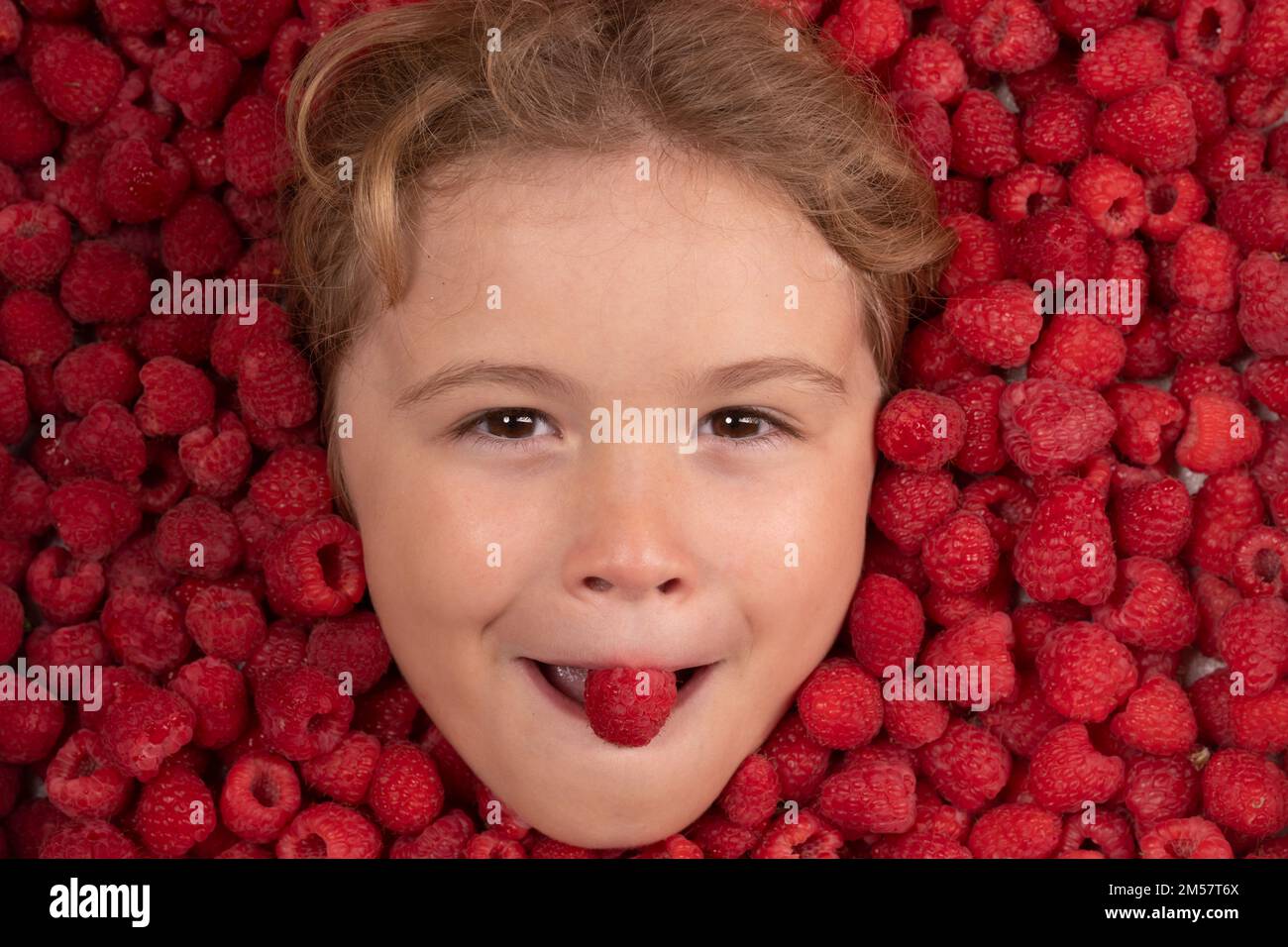 Funny kids face near raspberry background. Raspberry in kids mouth. The ...