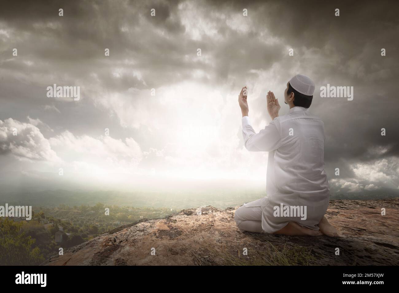 Rear view of a Muslim man sitting while raised hands and praying on the ...