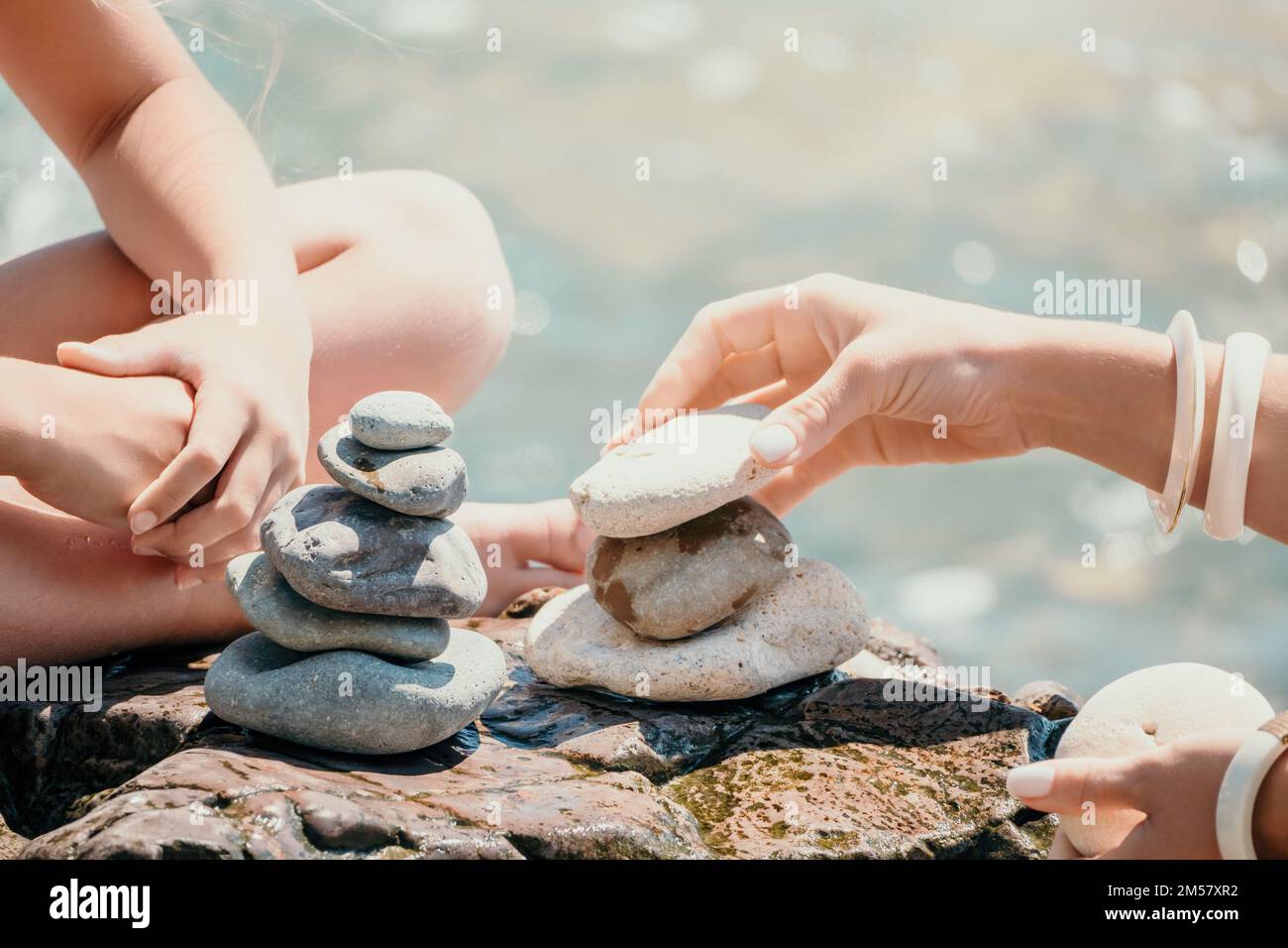Woman with daughter bilds stones pyramid on seashore on a sunny day on ...