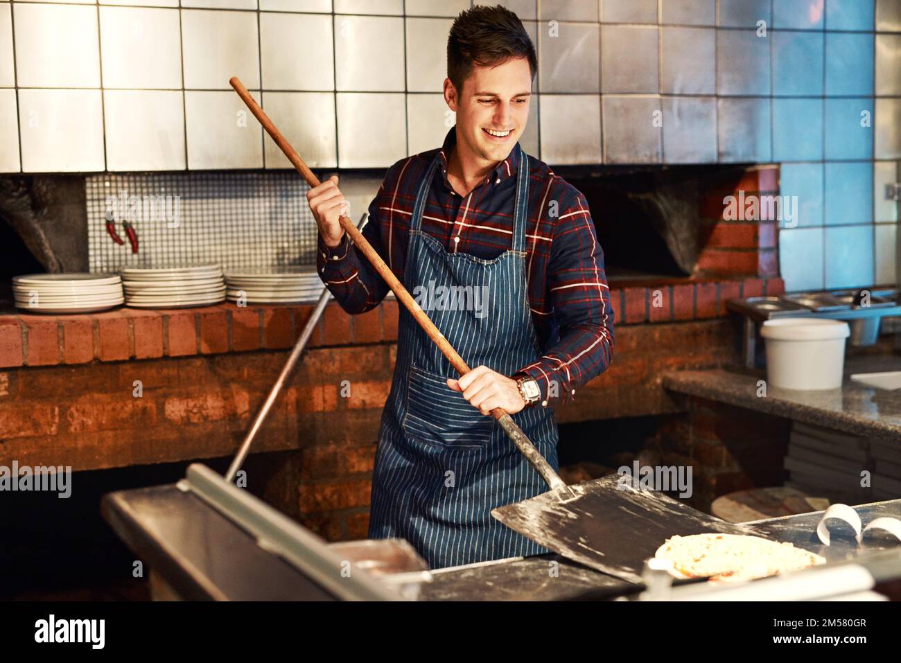 Hes a hands-on owner. a young man using a peel while making a pizza ...