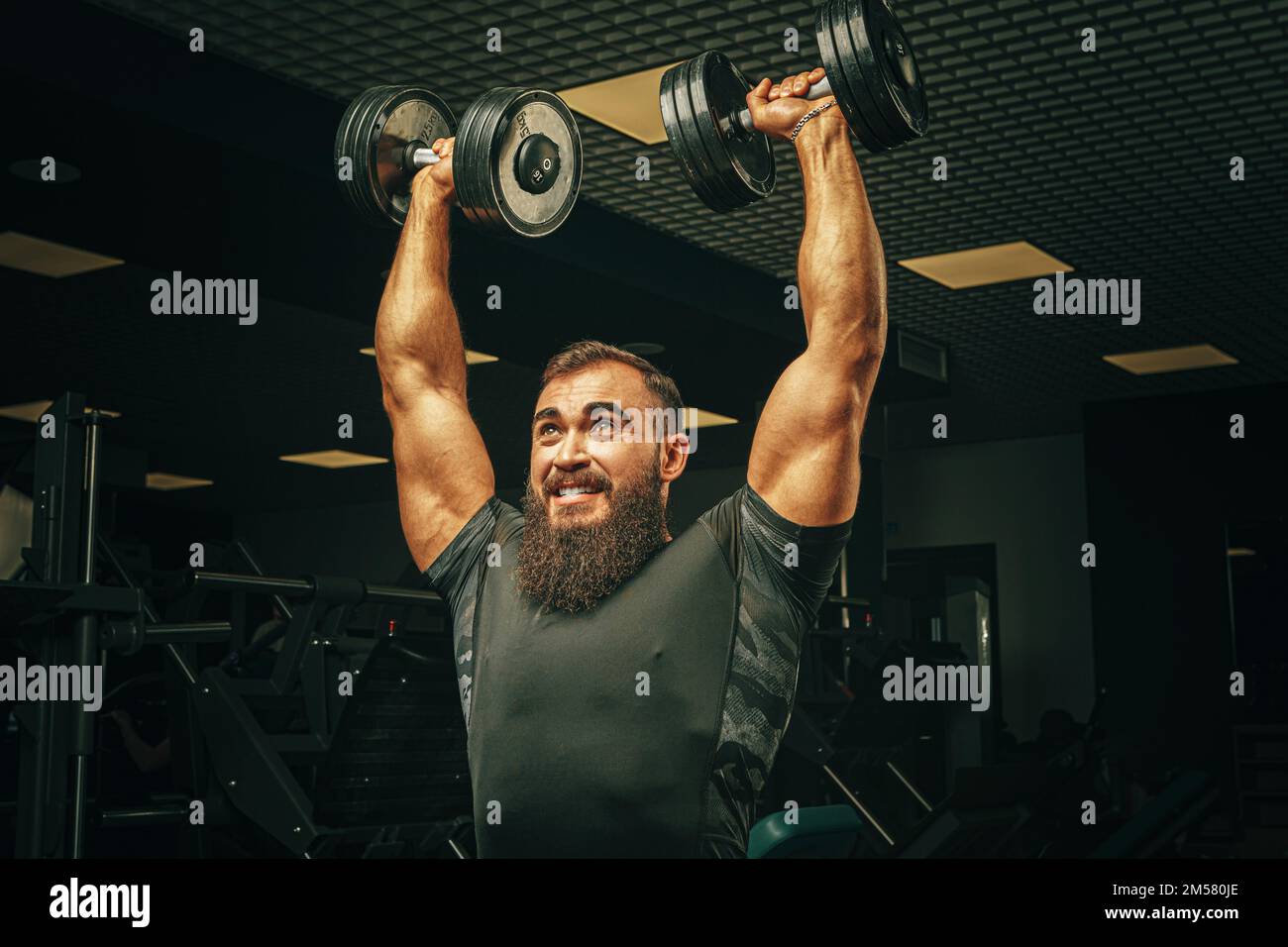 Muscular young man lifting weights in a dark gym Stock Photo - Alamy