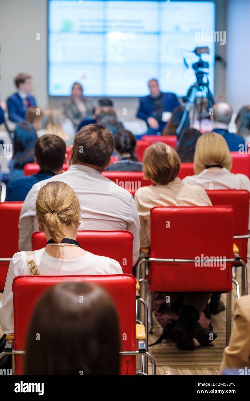 Anonymous people sitting on chairs in modern hall and listening to ...