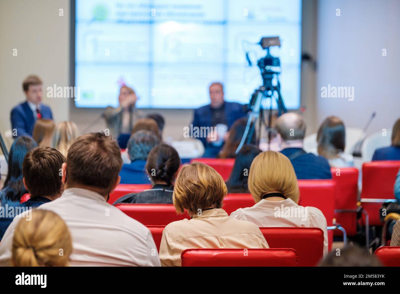 Anonymous people sitting on chairs in modern hall and listening to ...
