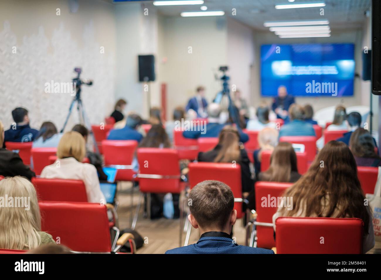 Anonymous people sitting on chairs in modern hall and listening to ...