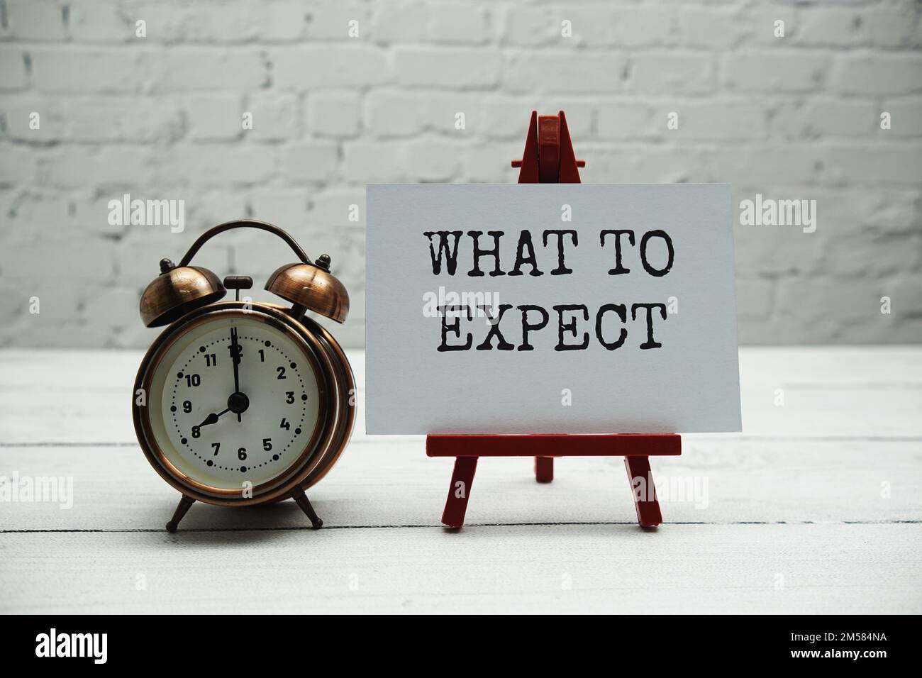 What to Expect? text and alarm clock on white brick wall and wooden ...