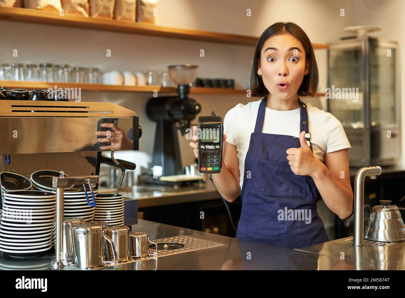 Portrait of cafe barista, girl shows thumbs up and card reader paying ...