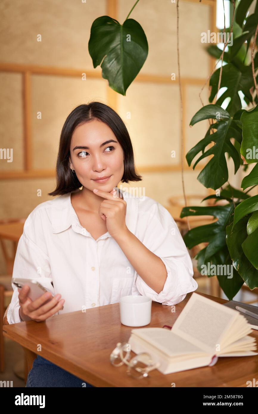 Beautiful young woman, 25 years old, thinking, holding smartphone and ...