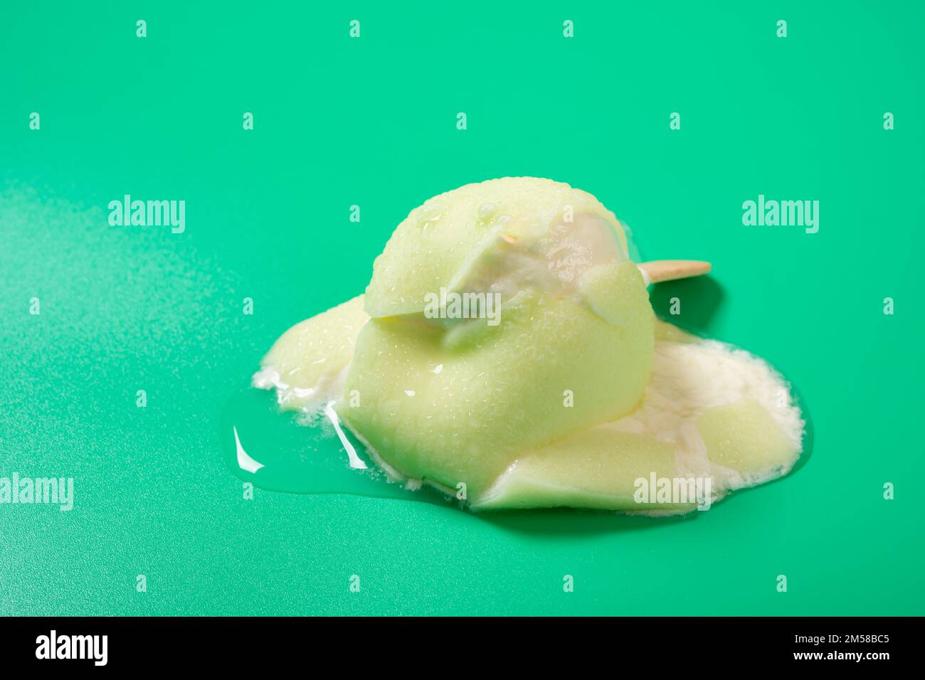 half melted green apple shape and flavor popsice on green background ...